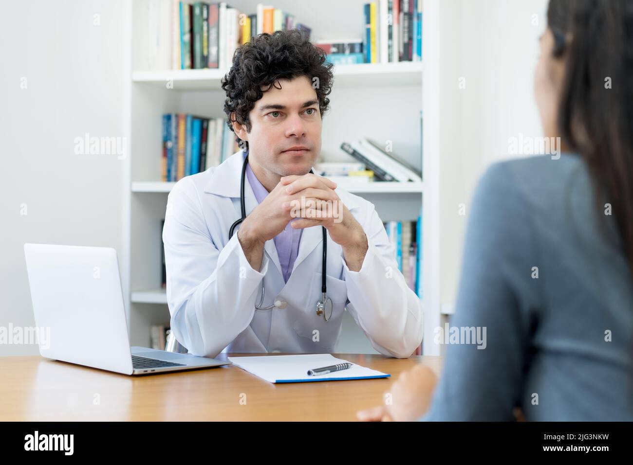 Likeable doctor listening to problems of female patient at office of ...