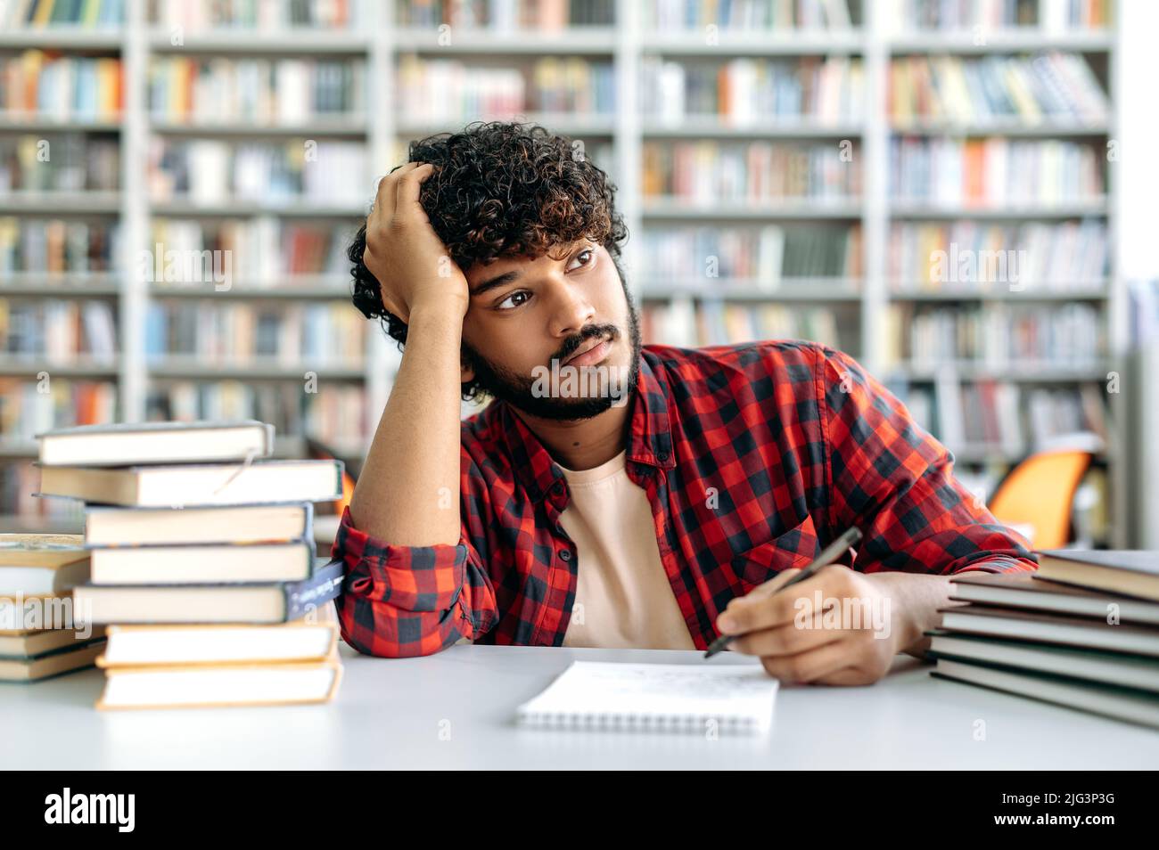 Sad arabian or indian male student tired from studying, sits at a desk ...