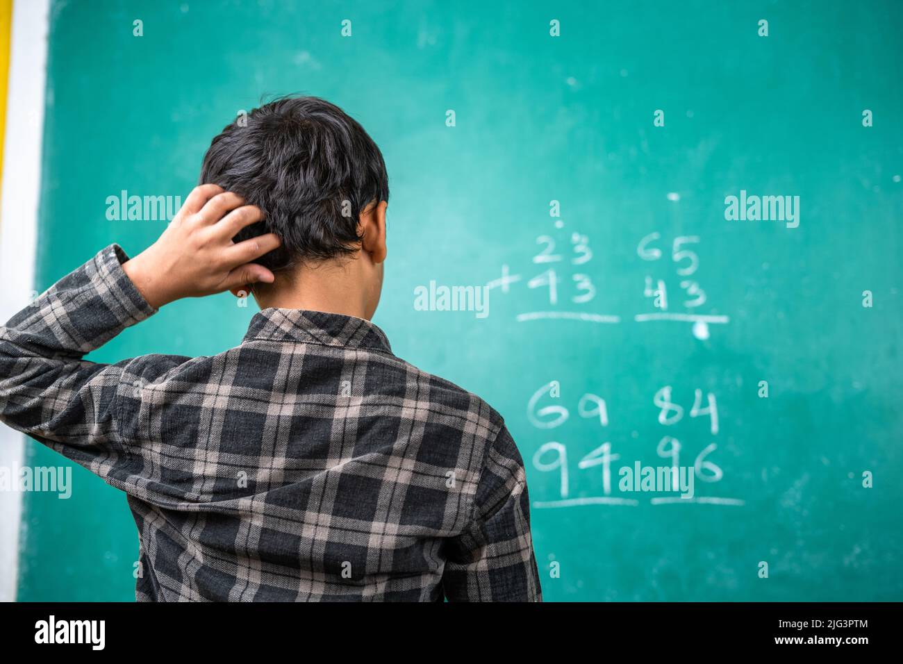 Confused kid scratching head to solve mathematics problem on board at ...