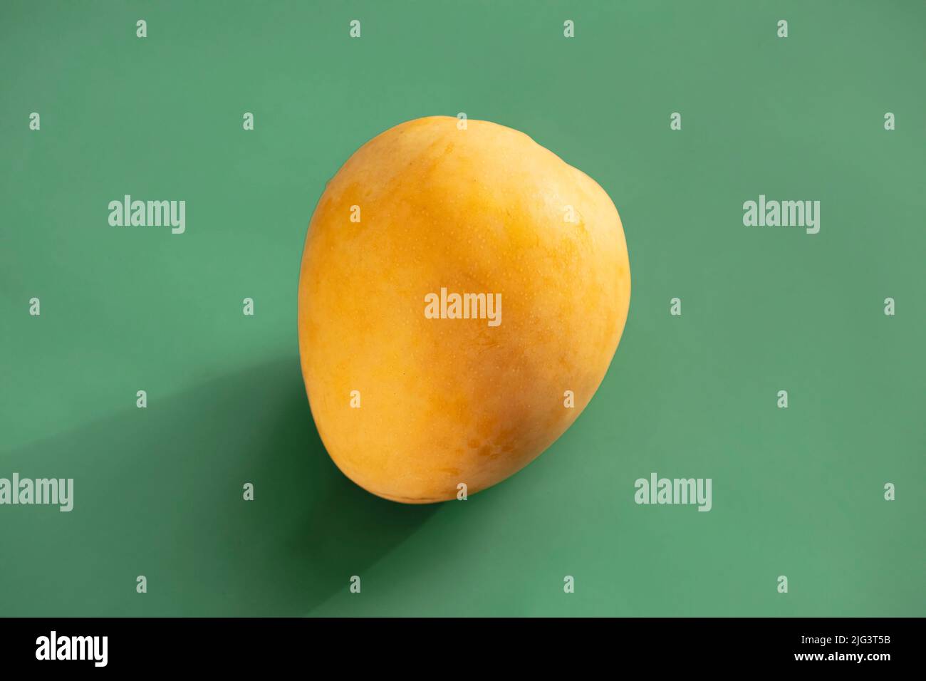 Sweet juicy ripe yellow mango on a green background under harsh shadow ...