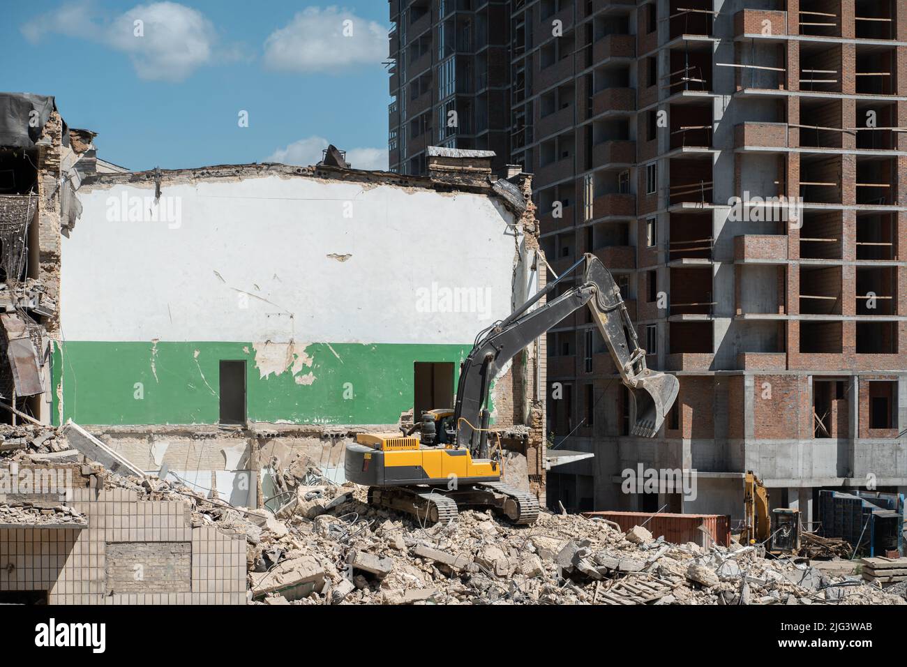 demolition old building by excavator near new construction of modern ...