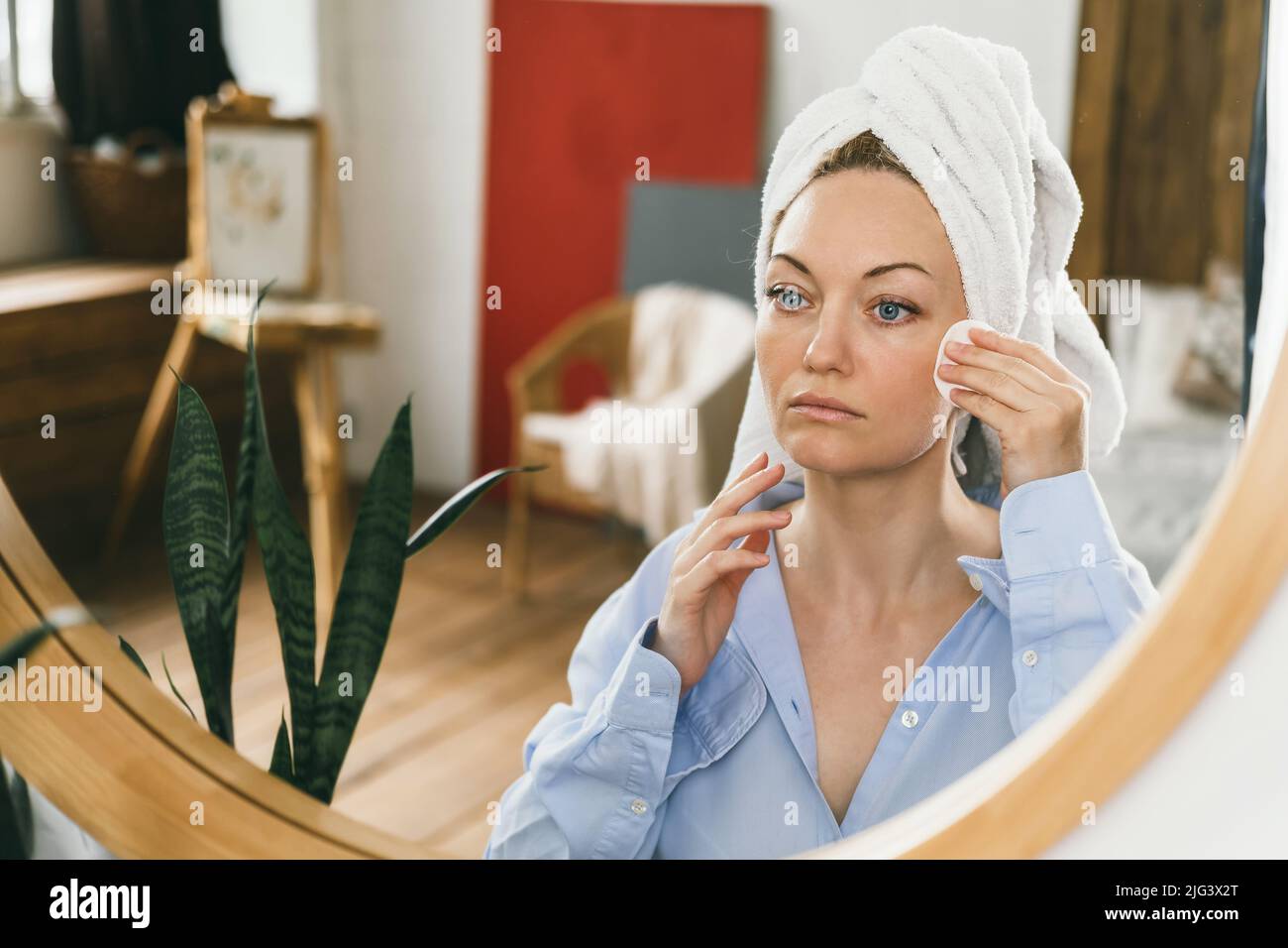 A beautiful woman in front of a mirror wipes her face with a cotton pad ...