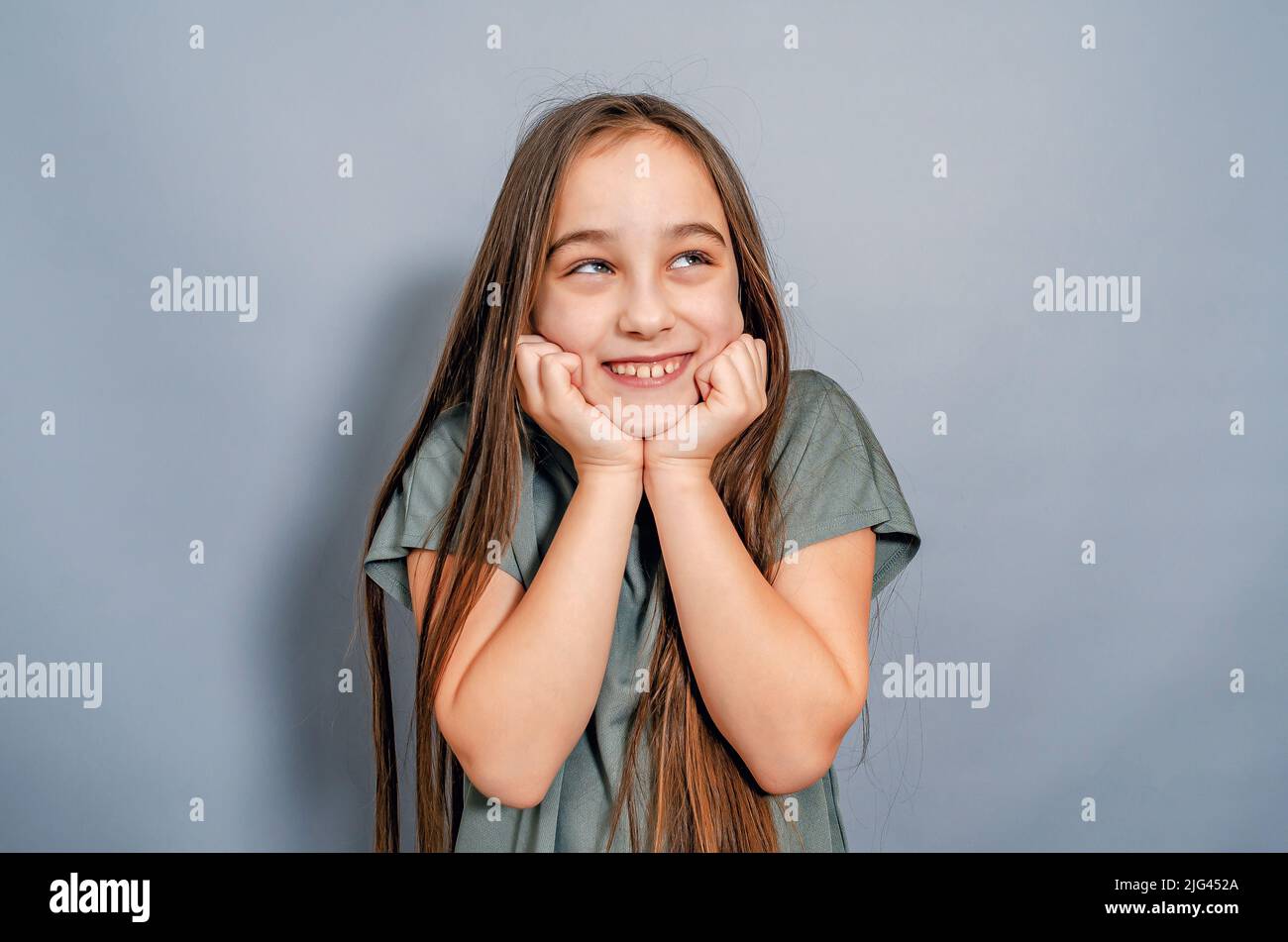 Playful little girl in gray T-shirt daydreamed. She is smiling, holding ...