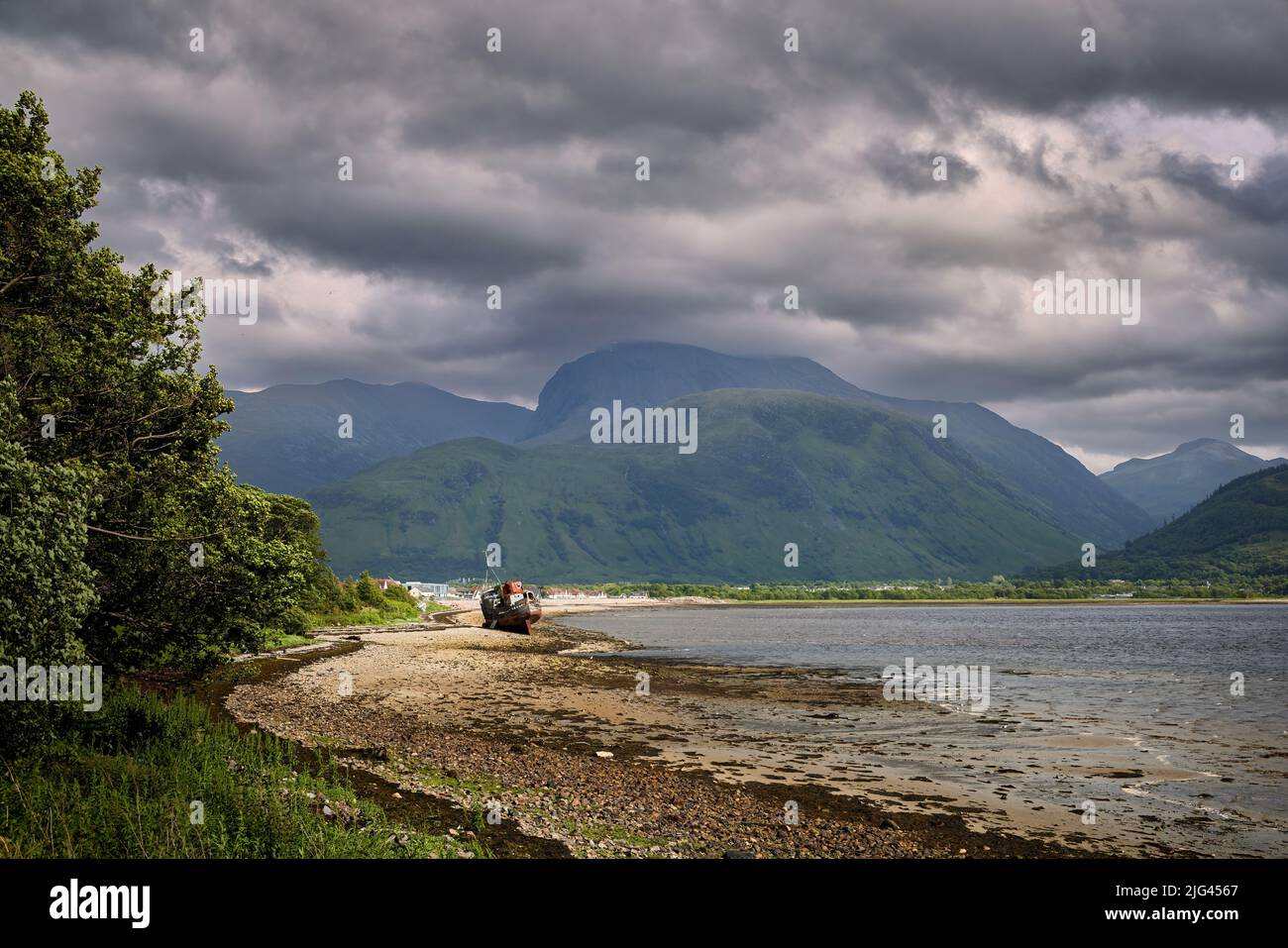 A wrecked fishing boat on the shore of Loch Linhe, the village of Caol ...