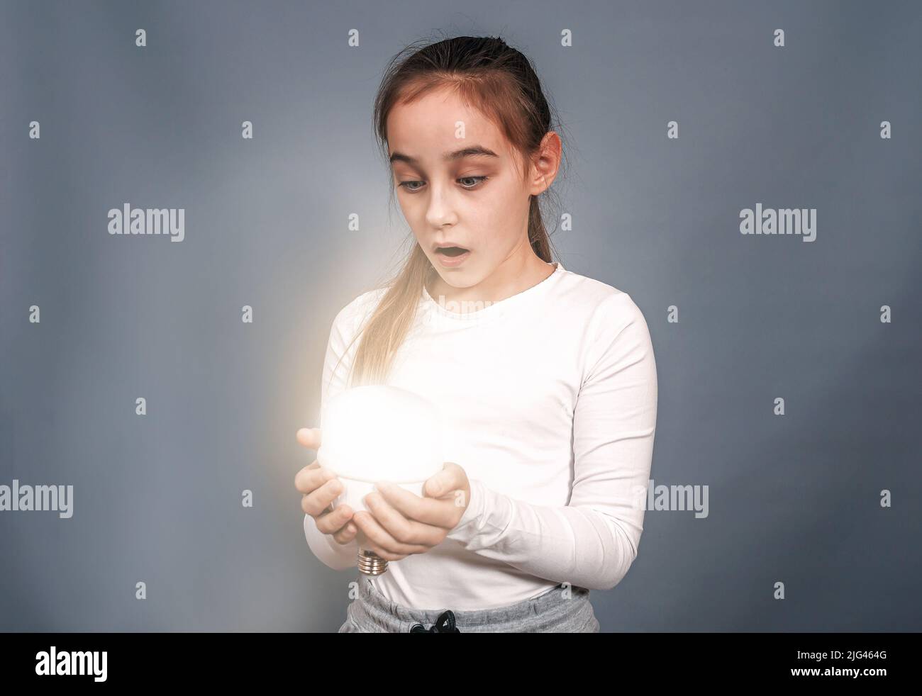 Surprised girl with glowing light bulb. Little girl in sportswear is ...