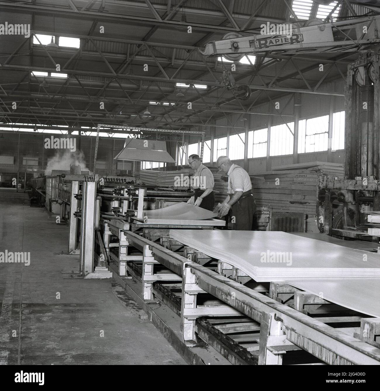1950s, historical, two steelworkers handling finished sheets of pressed ...