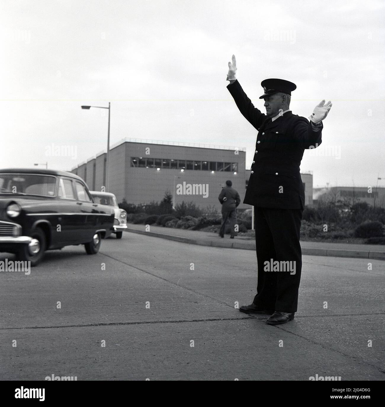 1950s, historical, uniformed security man signalling the cars leaving ...
