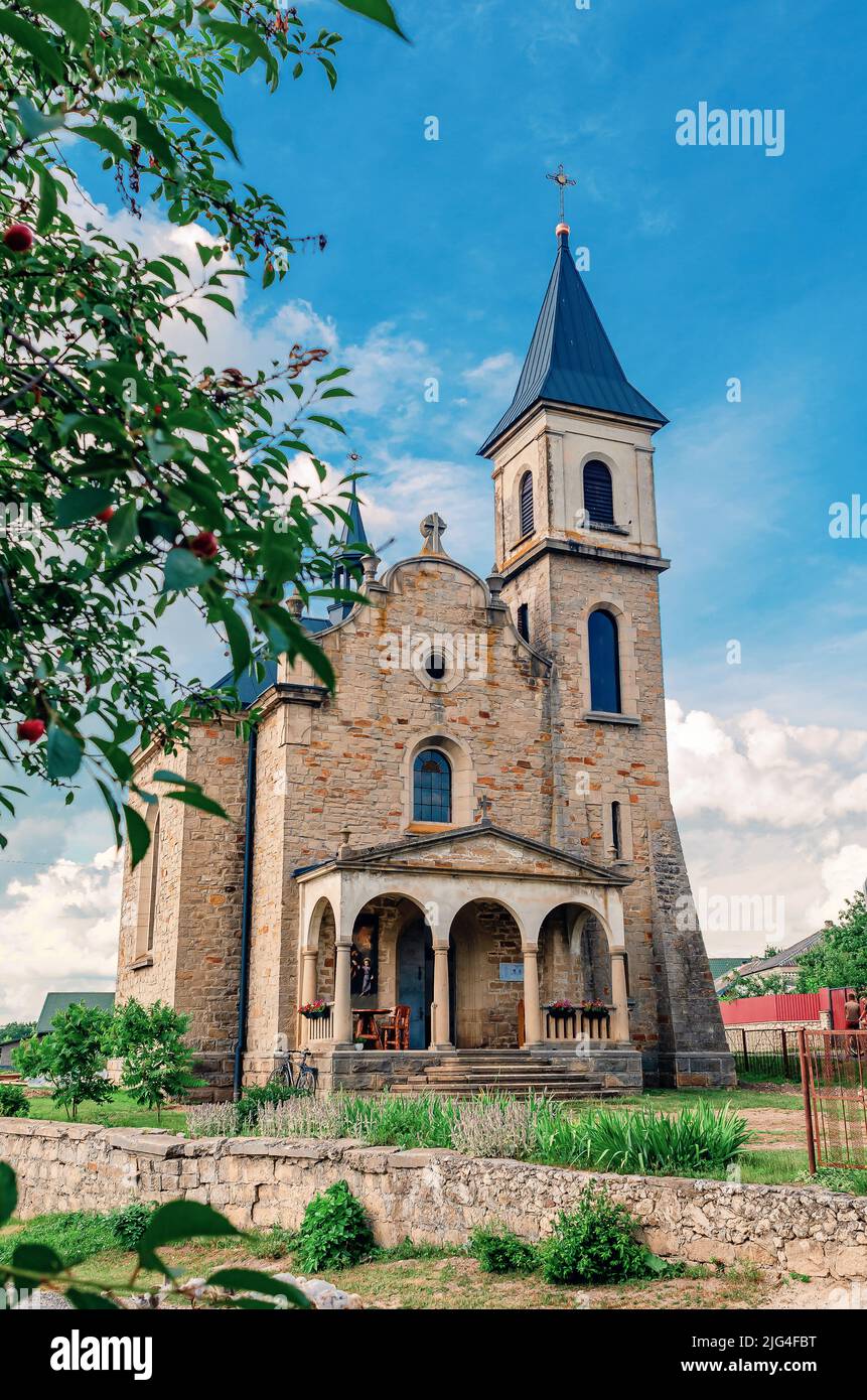 View of stone church through green branches of trees. Catholicism ...
