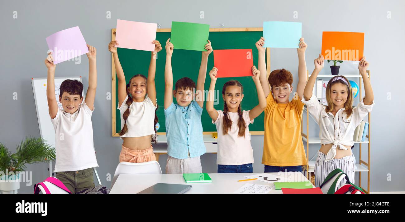 Happy elementary school boys and girls hold up colored paper sheets in ...