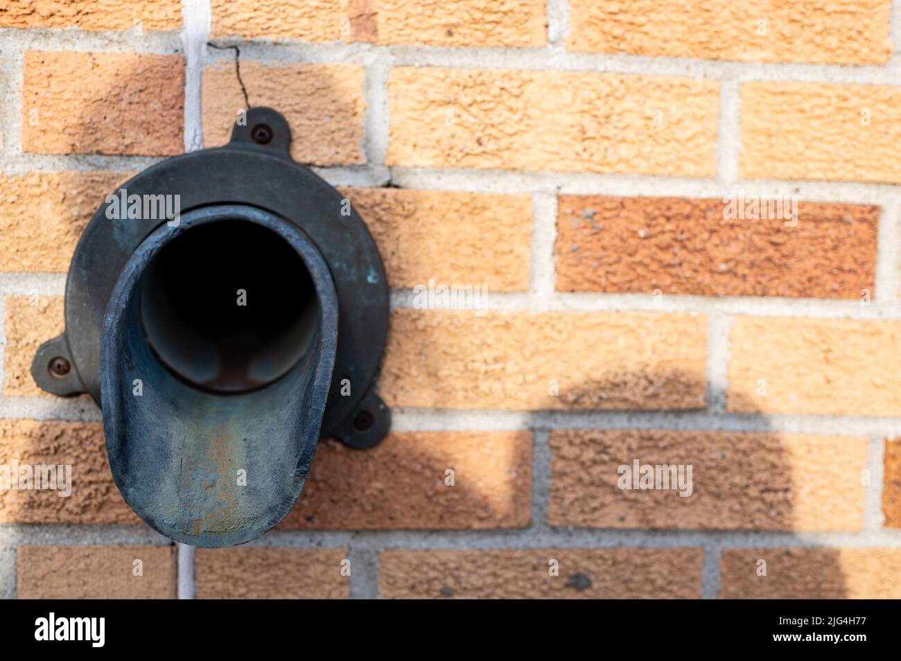 Brass metal down spout termination on the side of a brick building ...