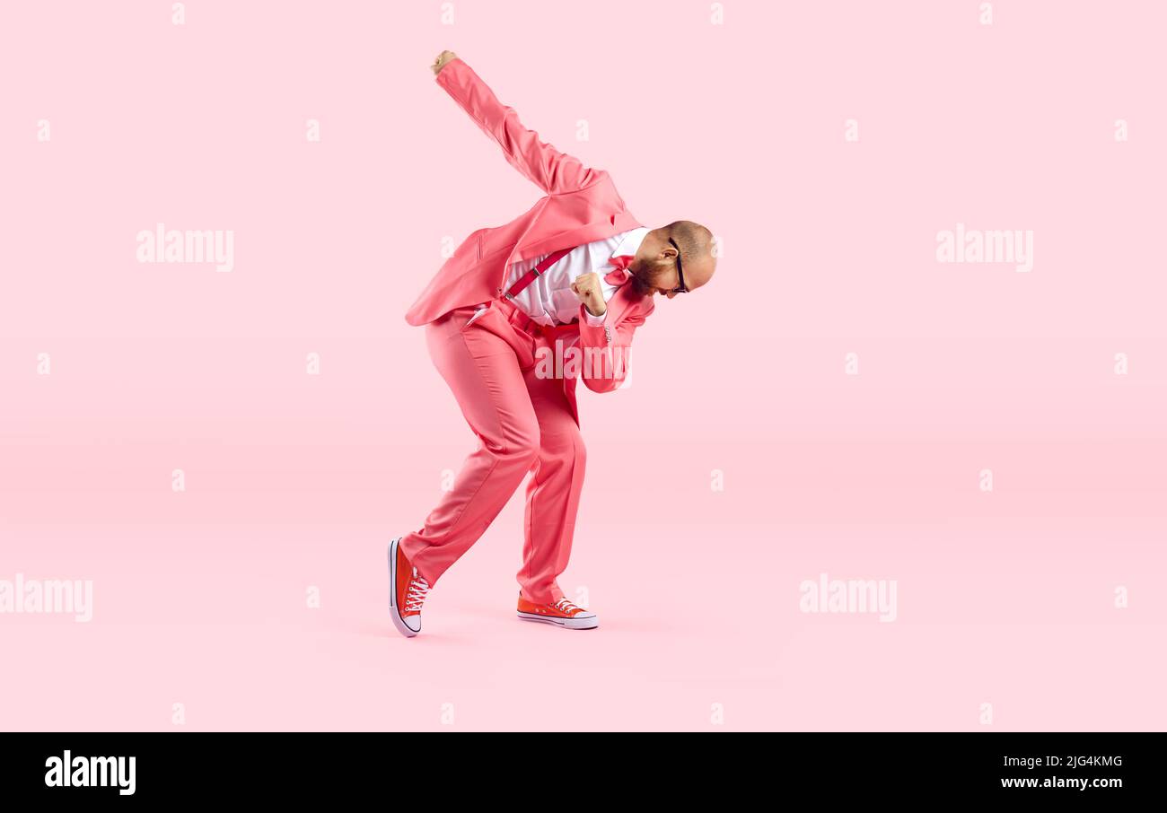 Funny young male dancer in pink suit and glasses dancing against pink ...