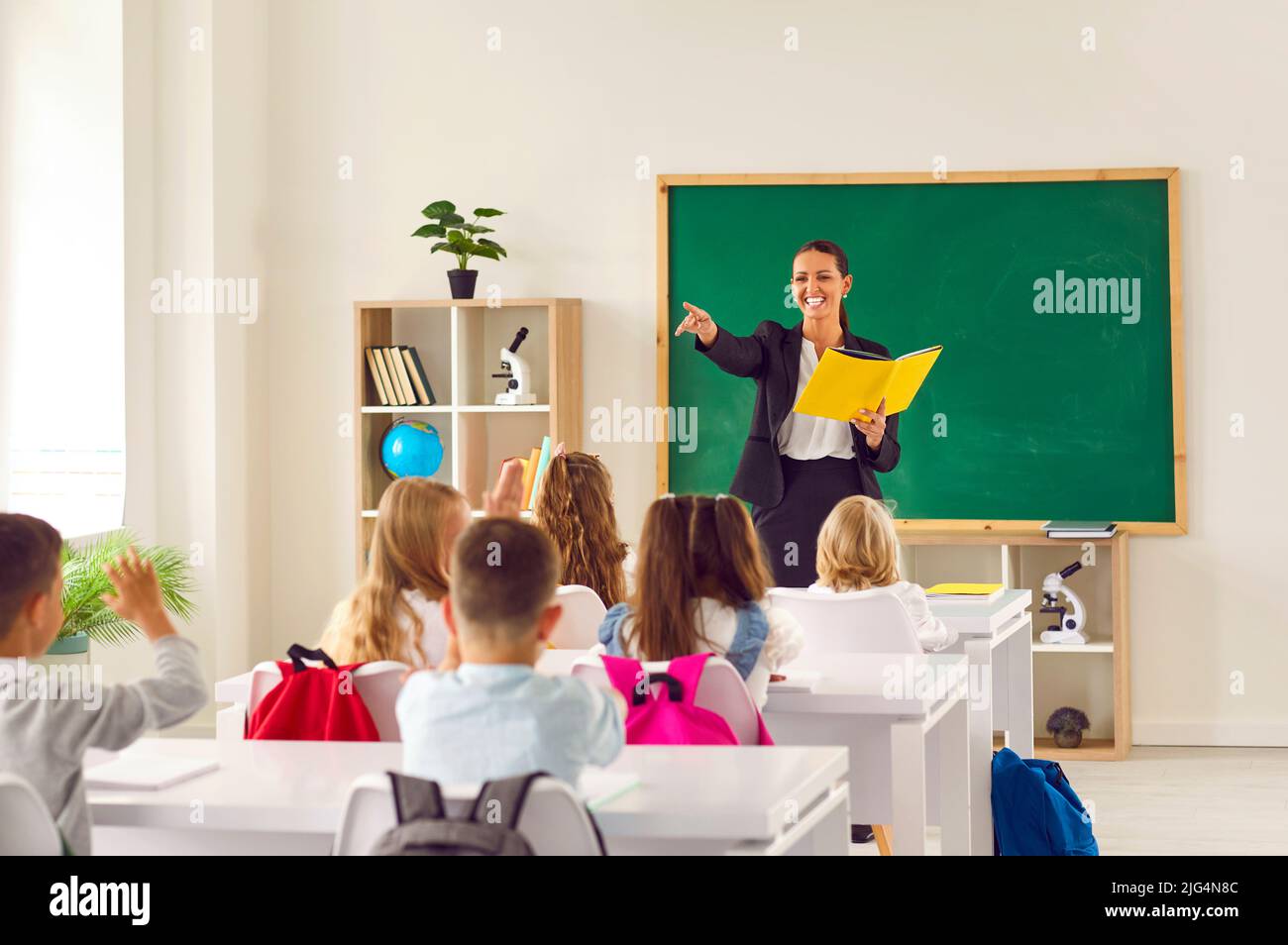 Friendly female teacher in classroom with book in her hands teaches ...