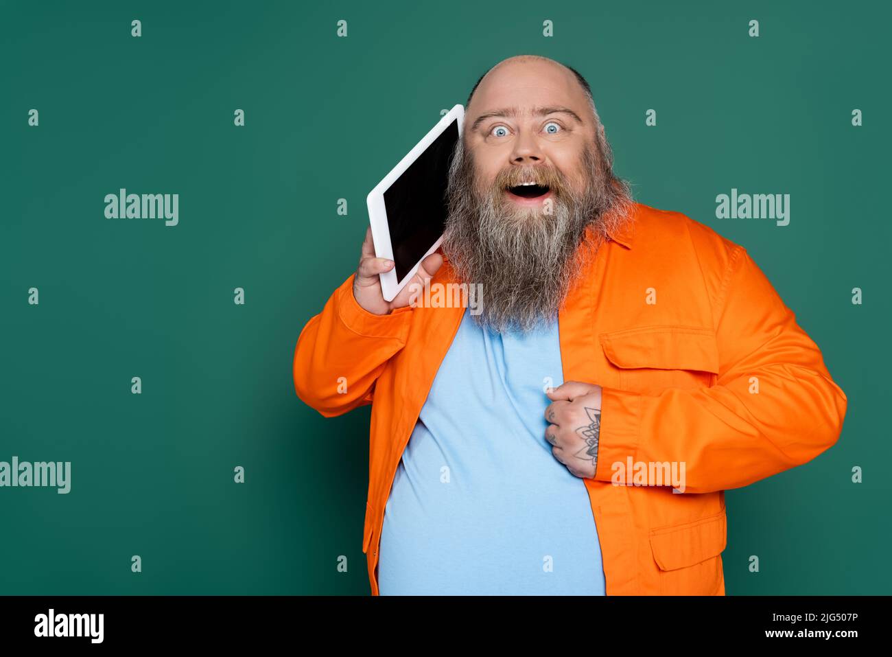 bearded astonished man with overweight holding digital tablet near face ...