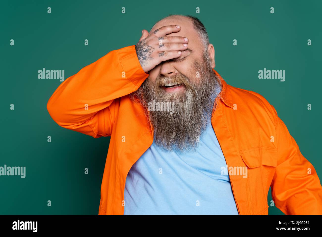 bearded overweight man laughing and covering eyes with hand isolated on ...