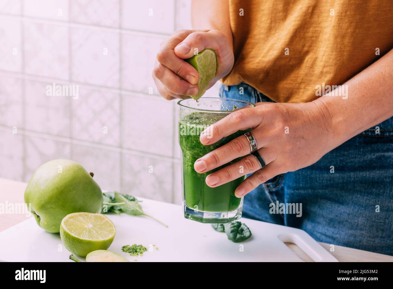 A woman prepares a green smoothie drink from fresh fruits and ...