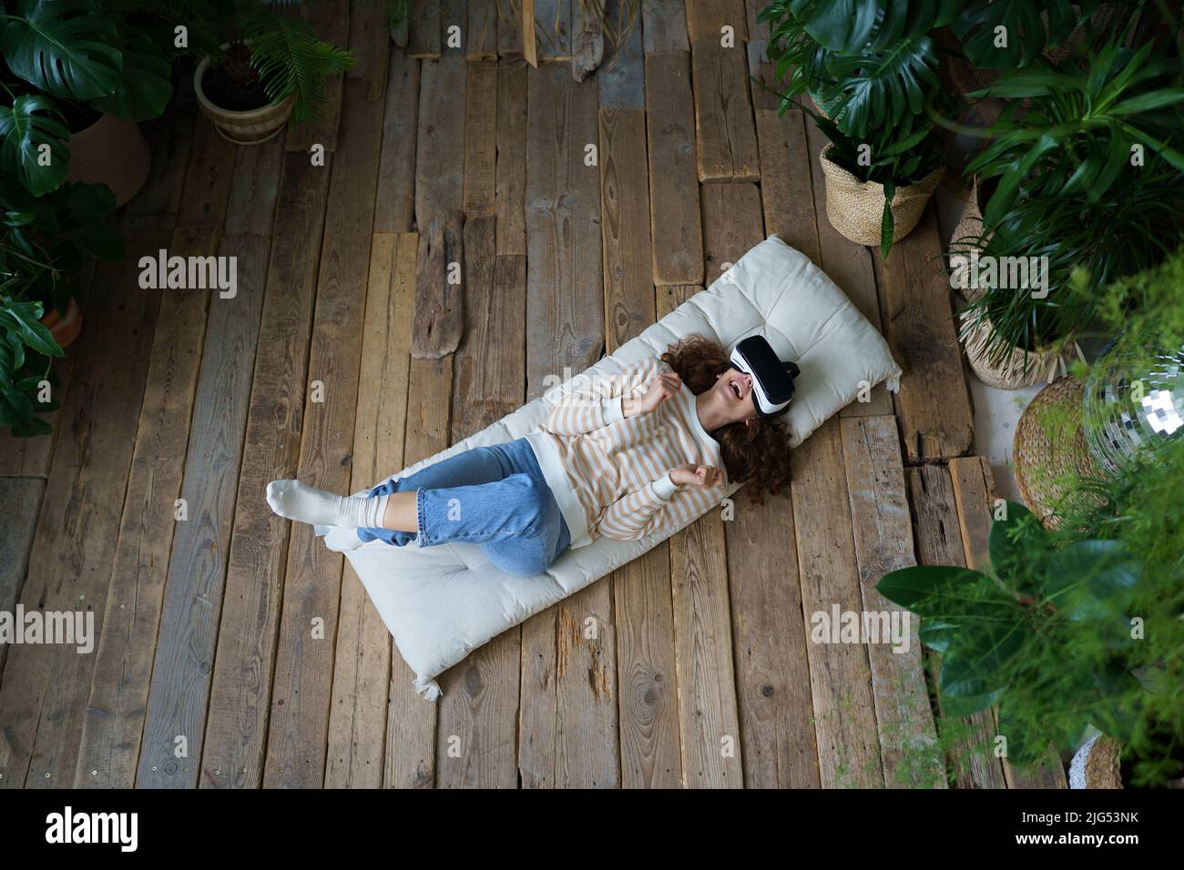 Young excited woman in VR helmet resting in greenhouse, lying on ...