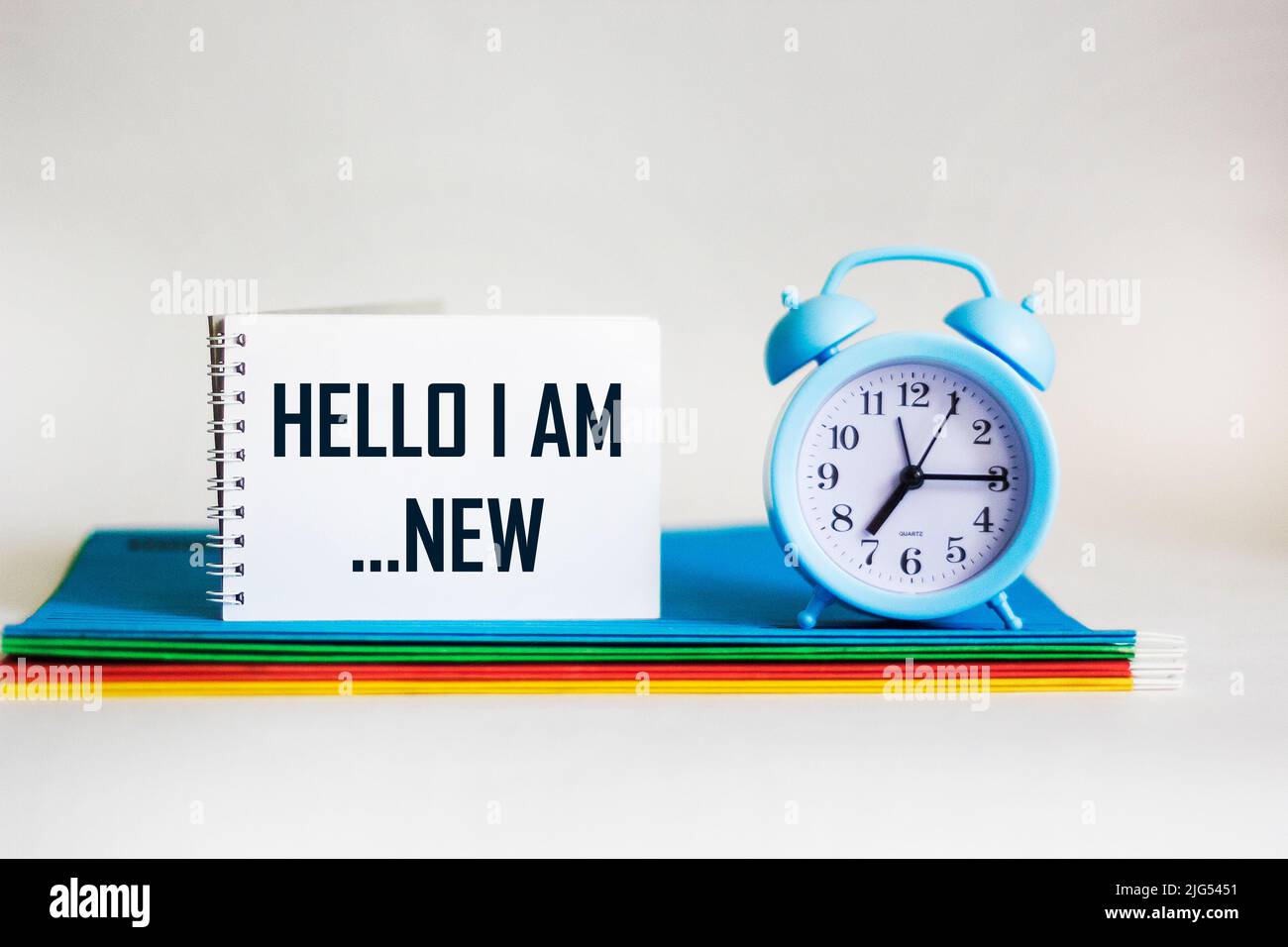 HELLO I AM NEW text on notepad with assorted folders and clock on white ...