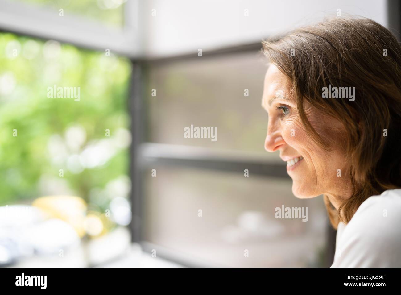 Side View Of Smiling Young Woman Looking Through Window At Home Stock ...