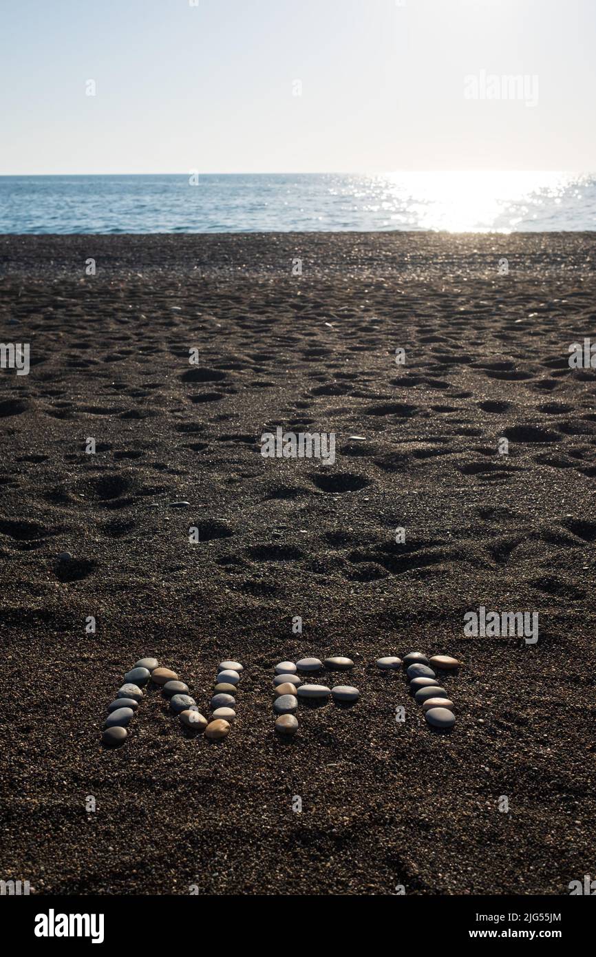 Concept of non-fungible NFT tokens. NFT text made from stones on beach ...