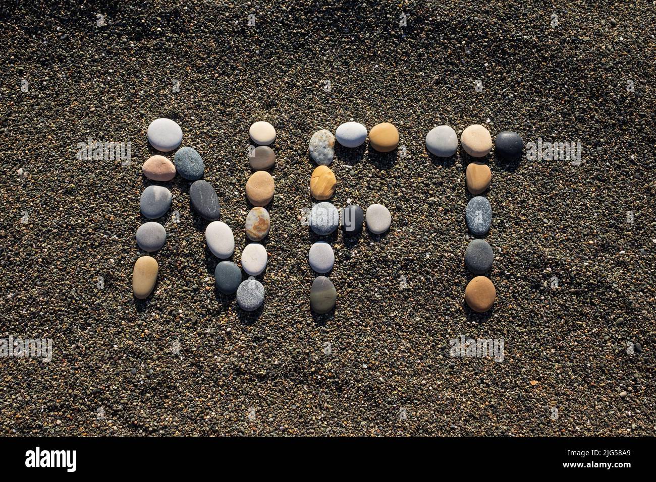 Concept of non-fungible NFT tokens. NFT text made from stones on beach ...