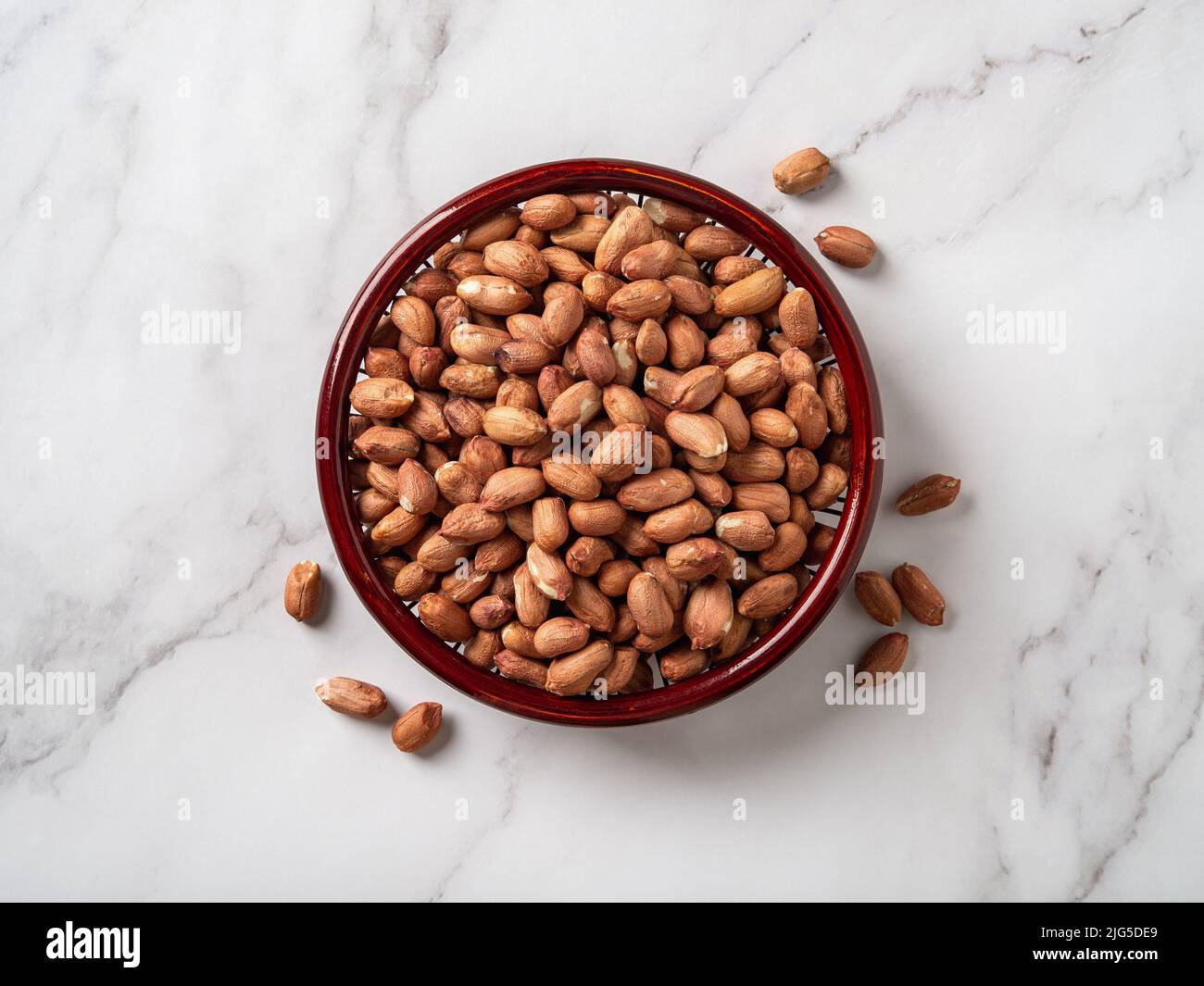 Raw peanut seeds in a wooden bowl on a marble countertop. Dried peeled ...