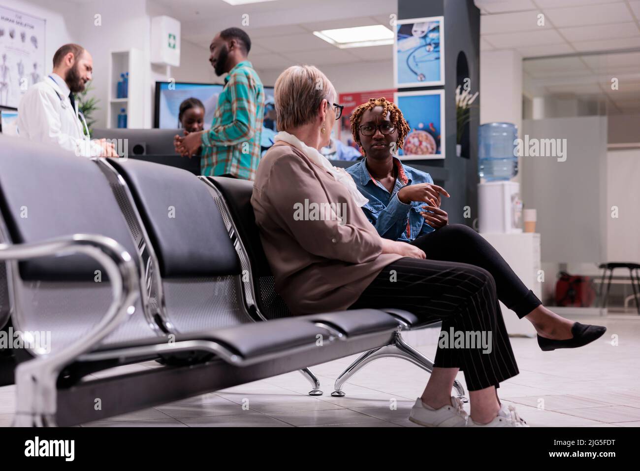 Diverse patients sitting in hospital reception waiting area, talking about medical appointment ...