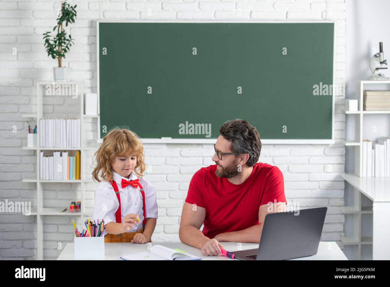 Elementary school boy in classroom on lesson. Teacher explaining to ...