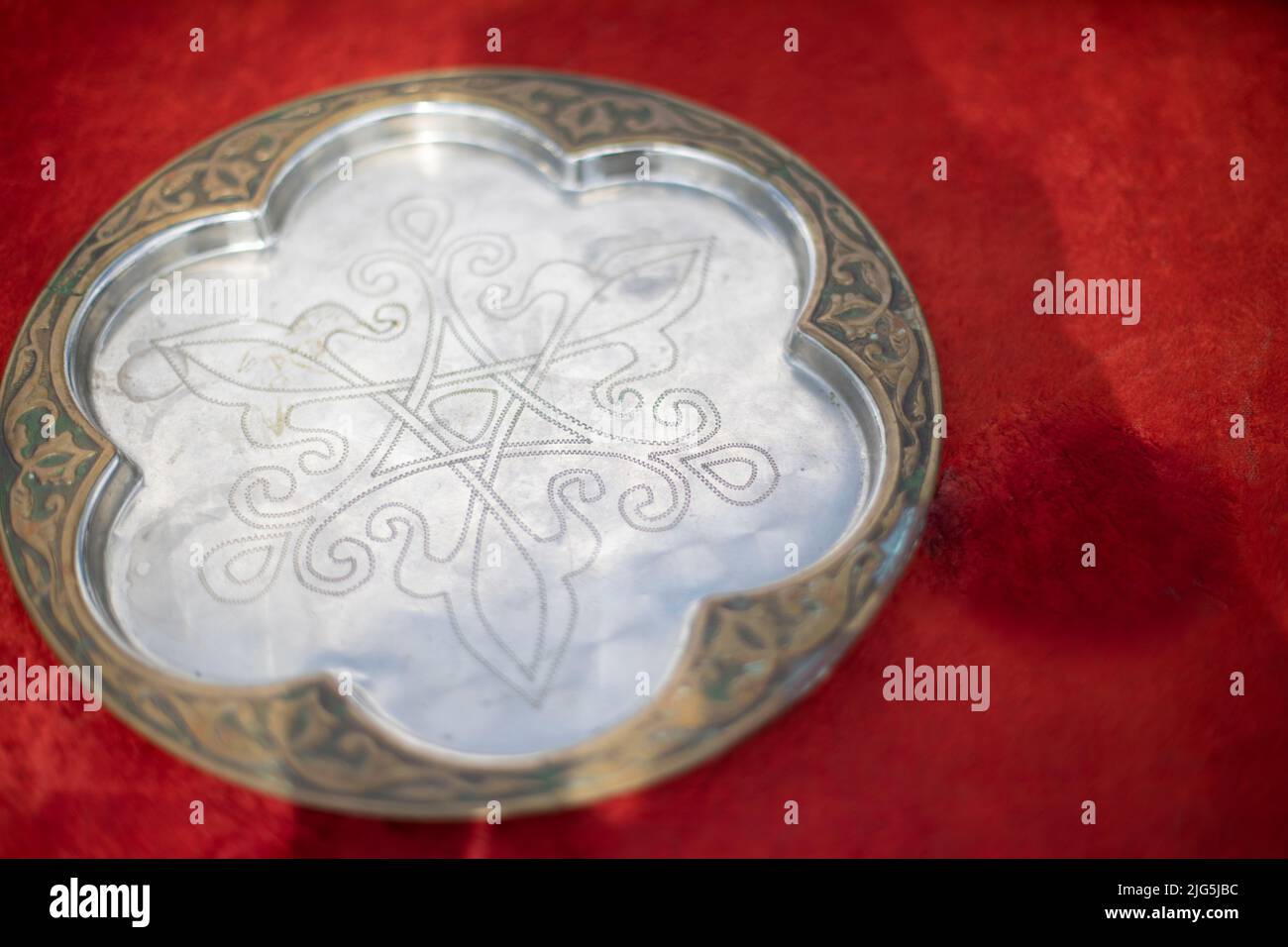 Steel dish with pattern. Plate on red cloth. Magician's inventory ...