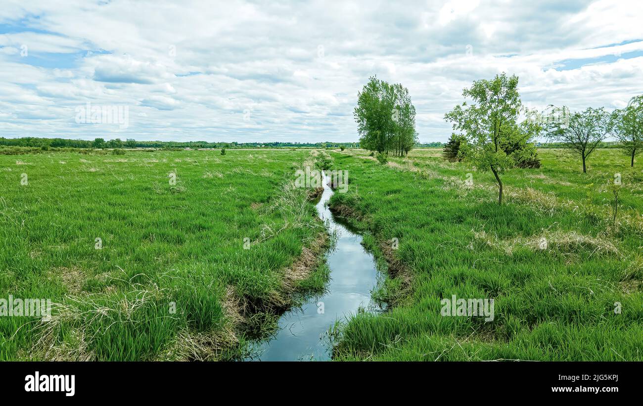 Springtime view of a small stream running through green fields under a ...