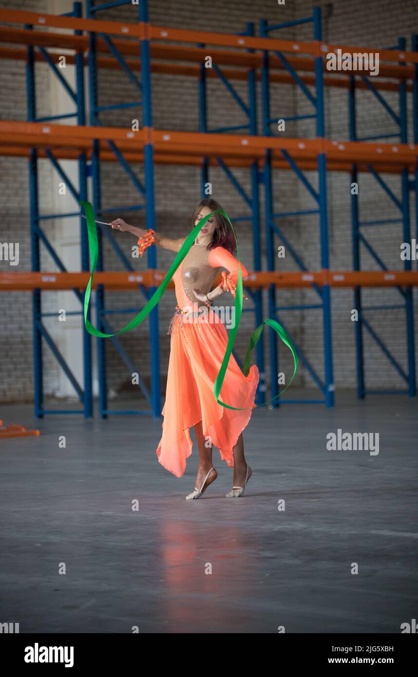 Young woman dancing with gymnastic ribbon in hands in the warehouse ...