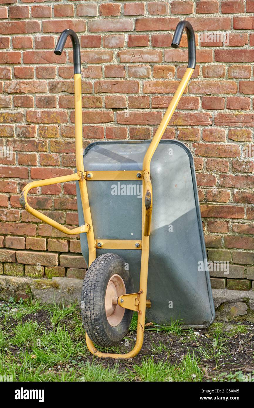 Garden wheelbarrow leaning against a red brick wall in a home backyard ...