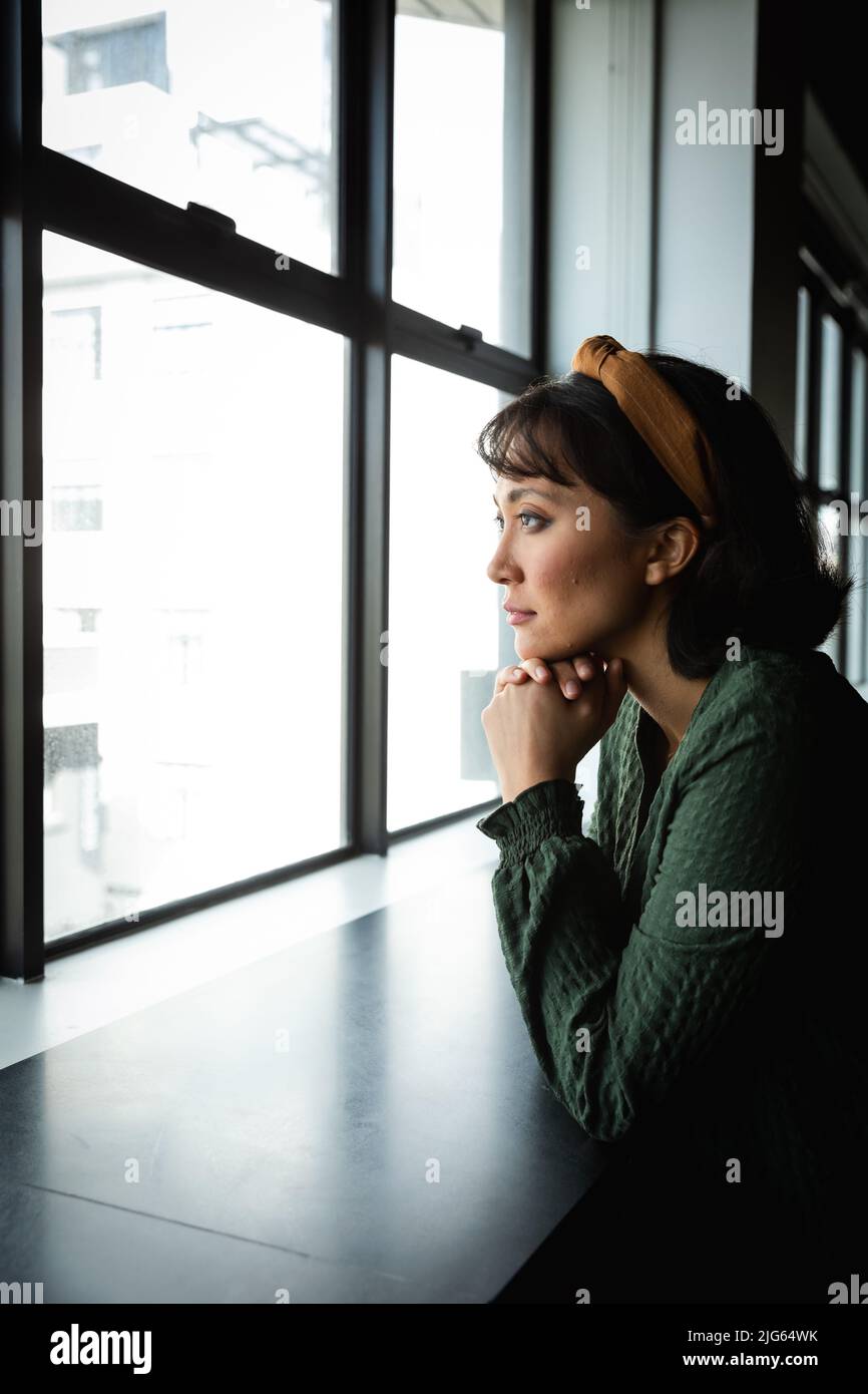 Thoughtful young asian businesswoman with hand on chin looking through ...