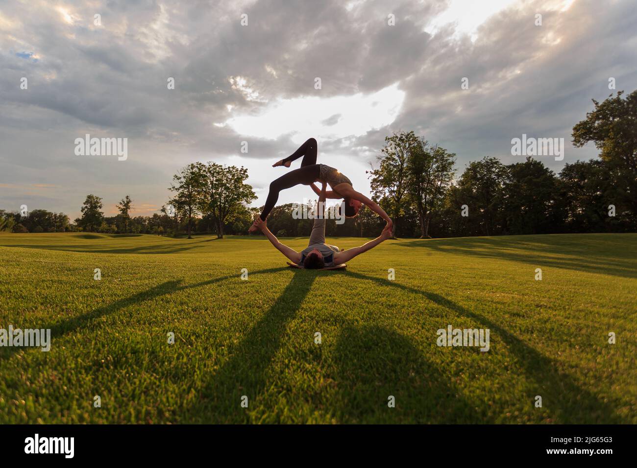 Young couple doing acro yoga in park. Man lying on grass and balancing ...