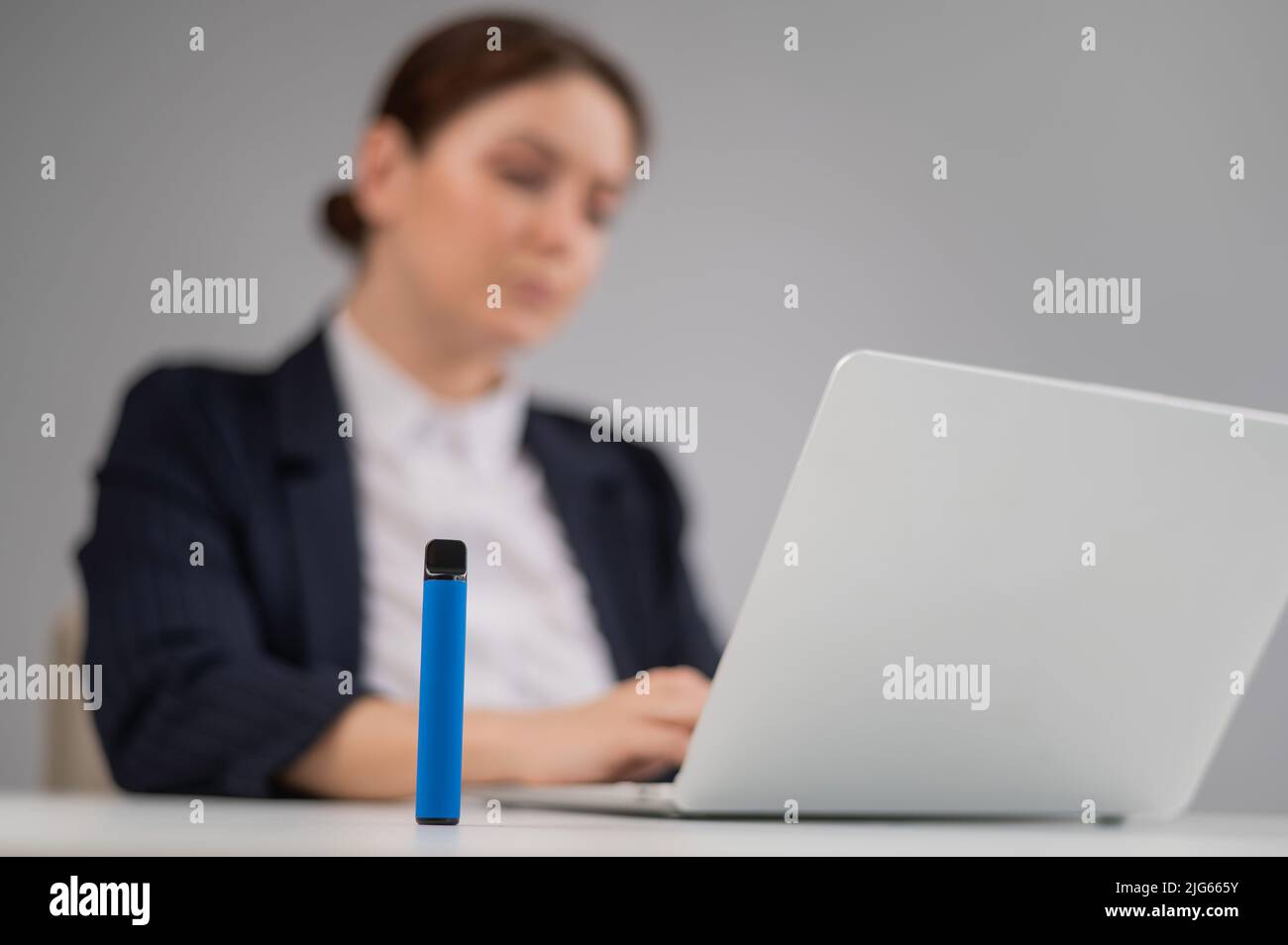 Business woman smoking a disposable vape while sitting at her desk ...