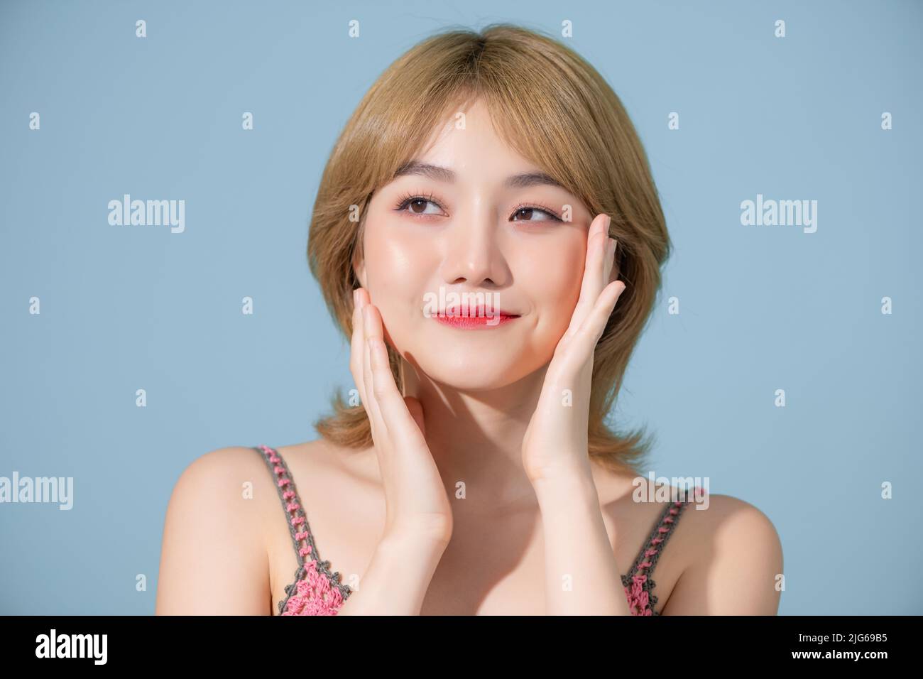 Happy young asian woman over pastel blue background touches both cheeks ...
