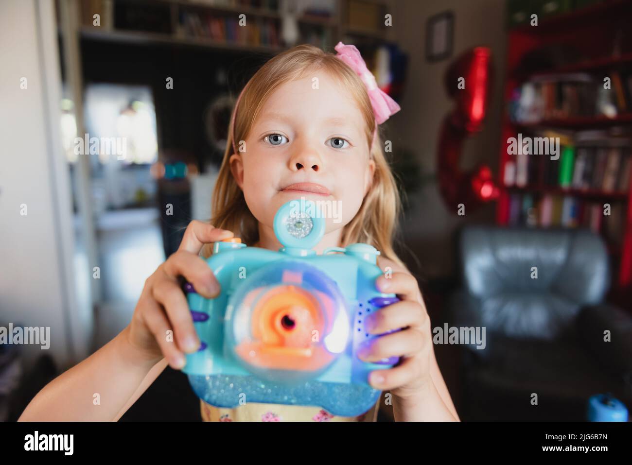 Blond girl playing with toy photo camera in living room. Funny little ...