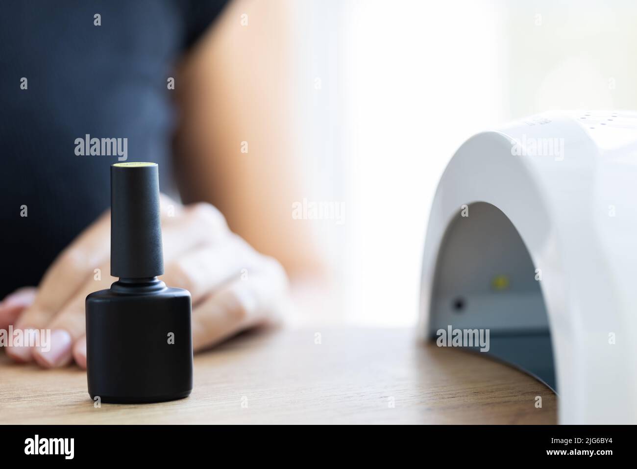 Black bottle of shellac gel near uv lamp with womans hand behind ...