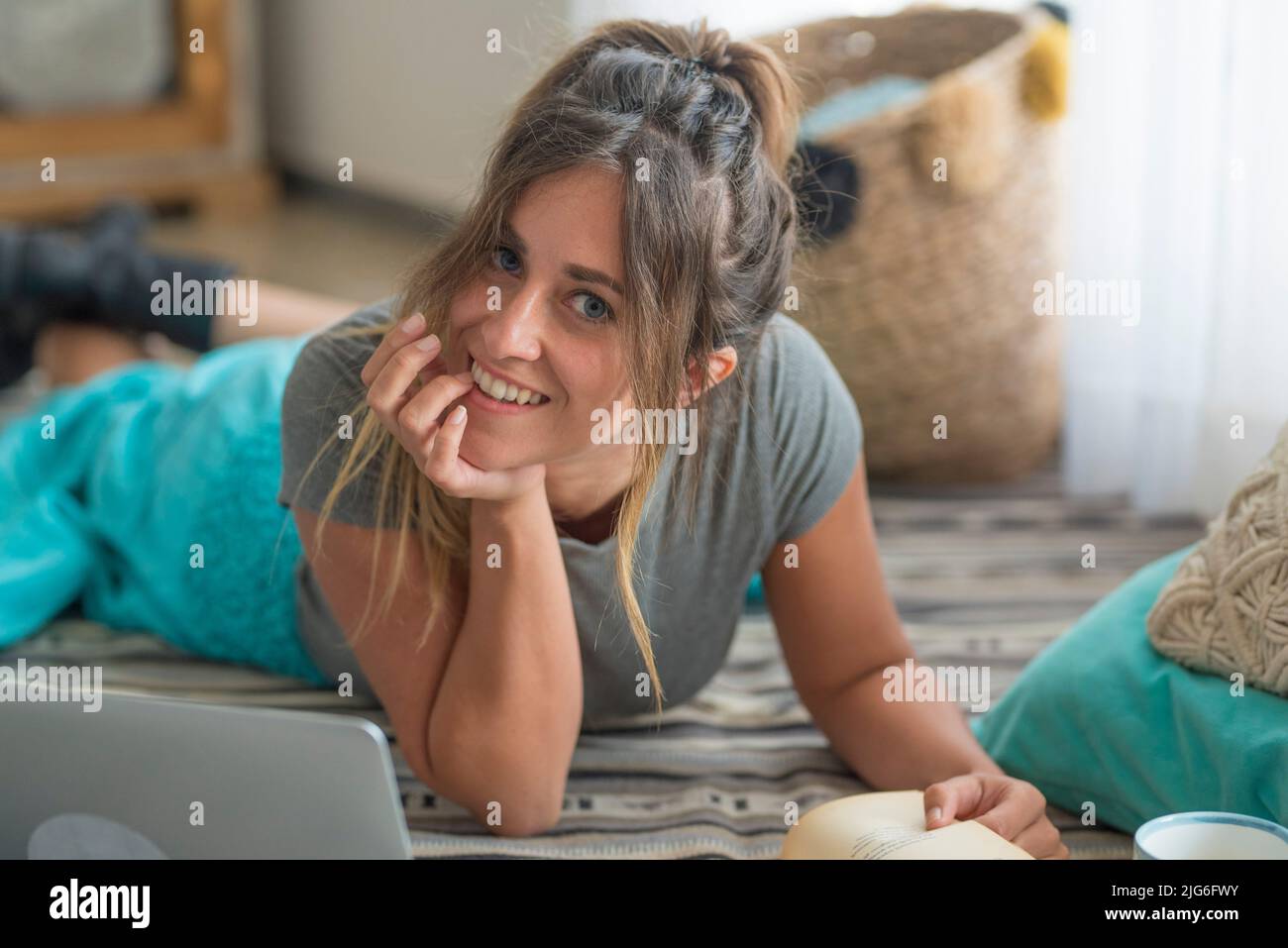 Portrait of happy and cheerful young woman at home laying on the floor ...