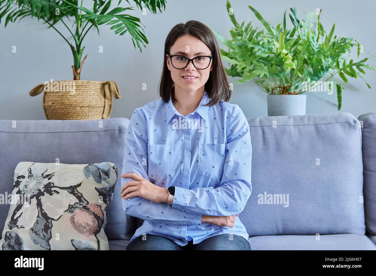 Young beautiful woman in glasses looking at camera sitting on sofa ...