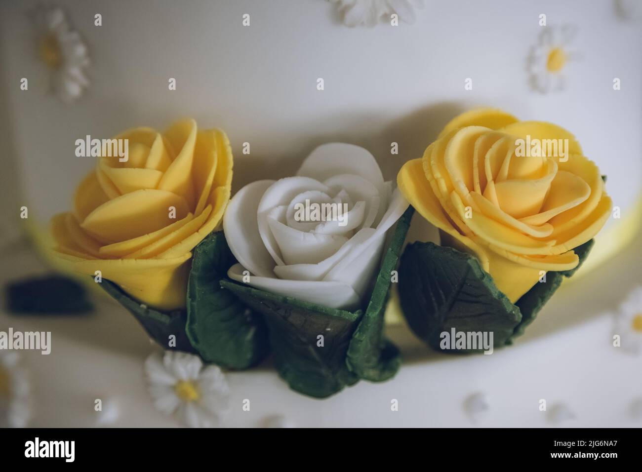 A close up of yellow and white roses on a wedding cake made from icing ...