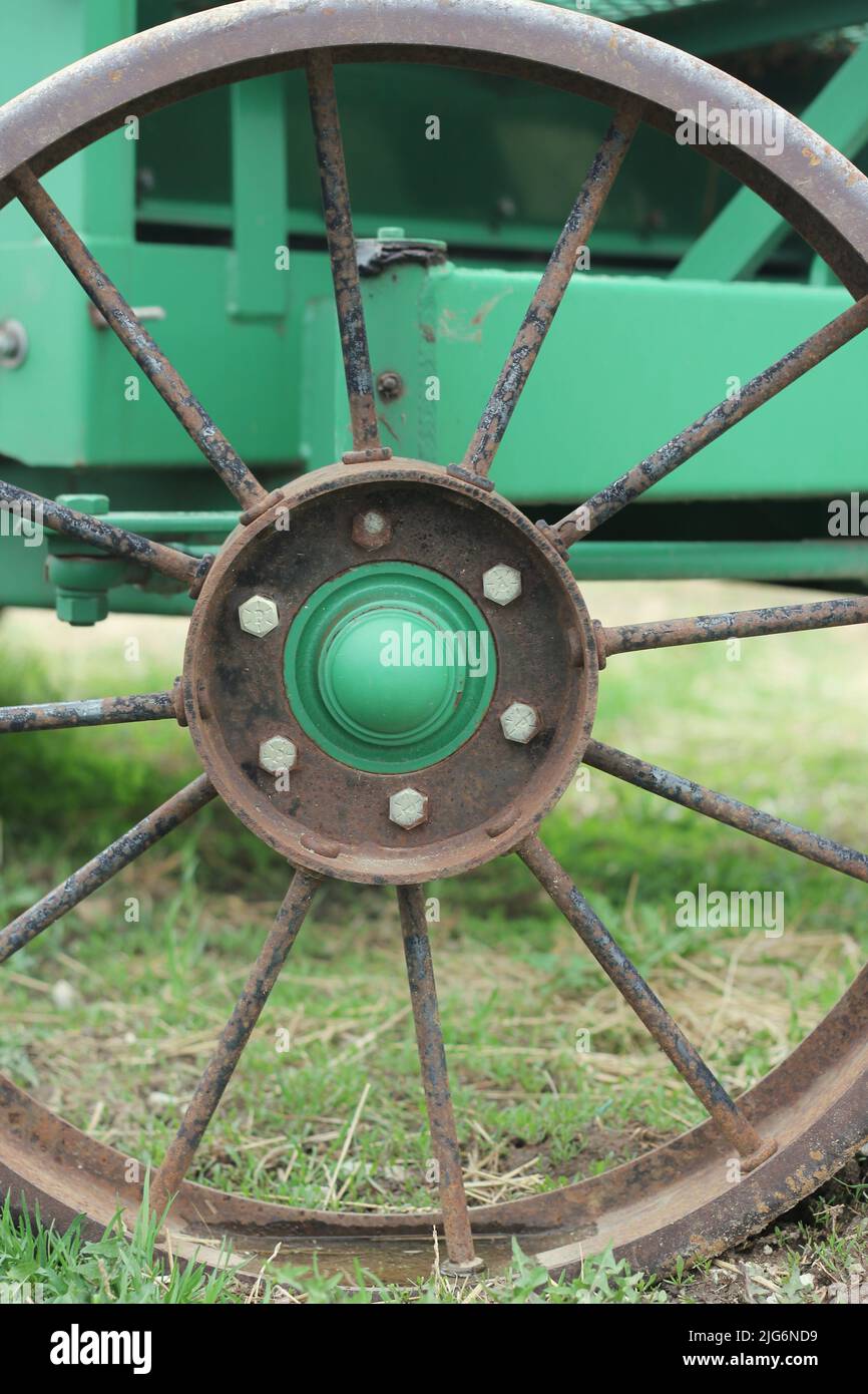 A vintage green metal tractor wheel with an axle and exposed spokes ...