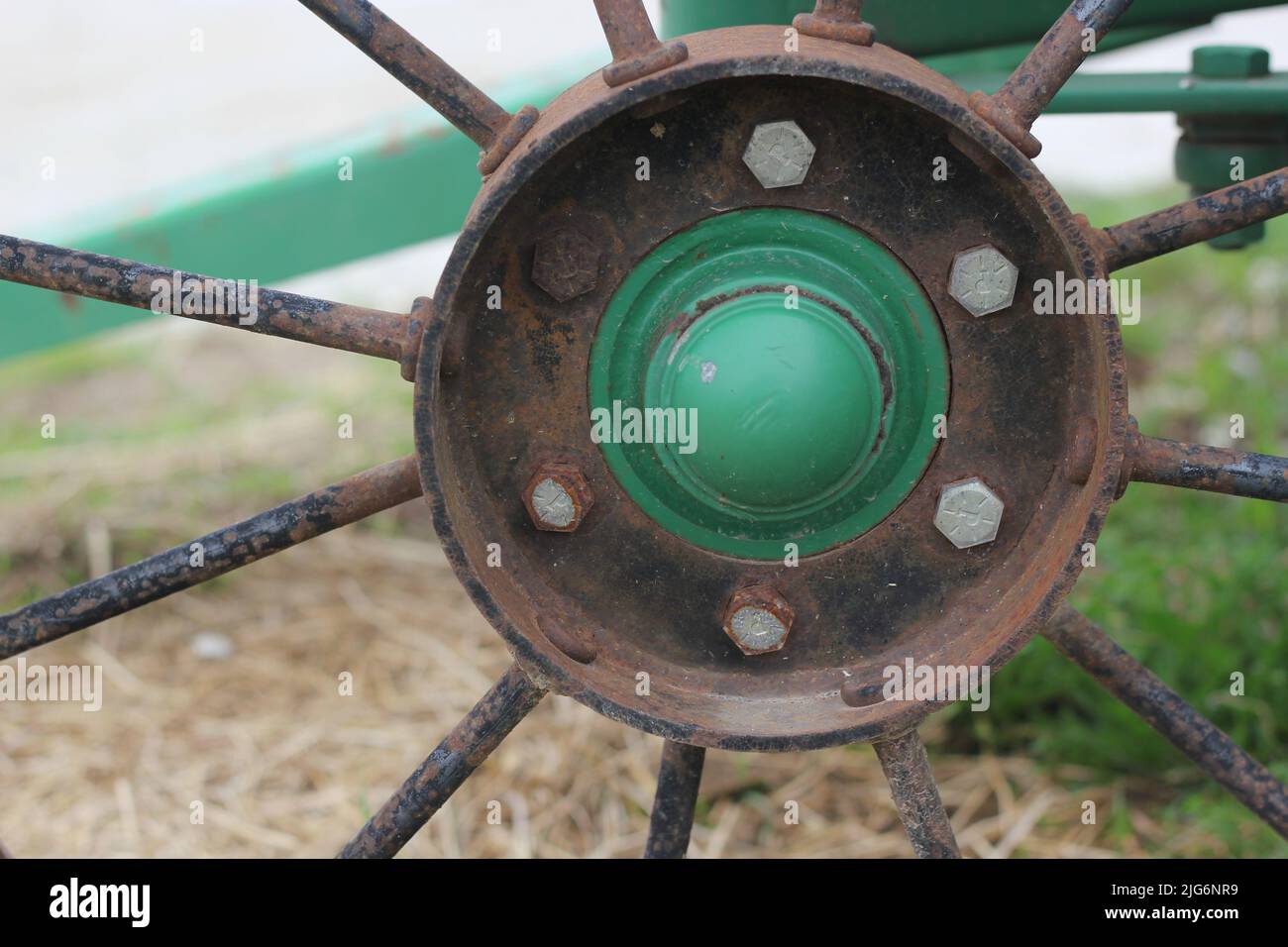 A vintage green metal tractor wheel with an axle and exposed spokes ...