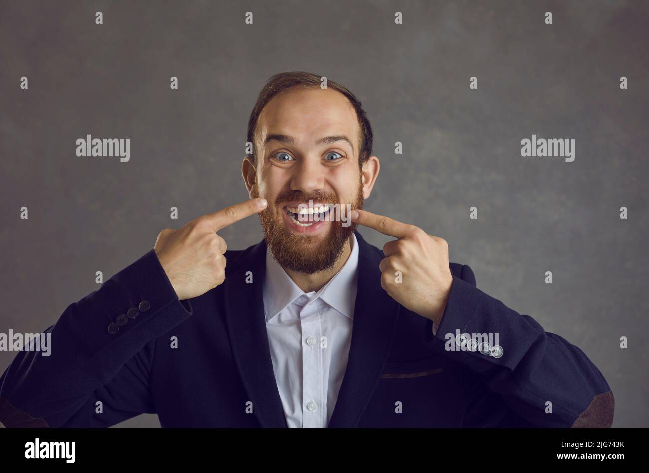 Studio portrait of a happy young man pointing at his smile with natural ...