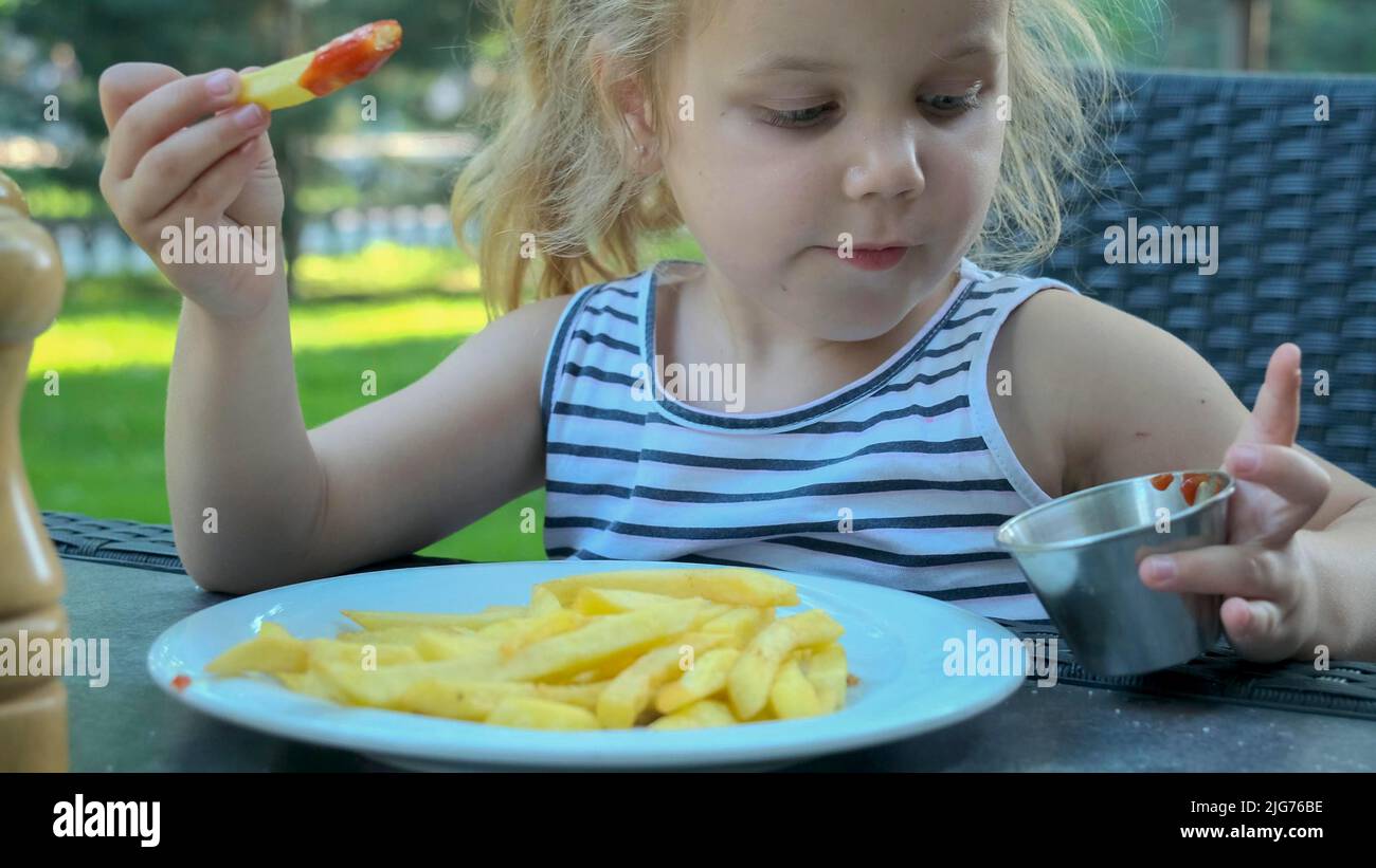 Little girl eat french fries. Close-up of blonde girl takes potato ...