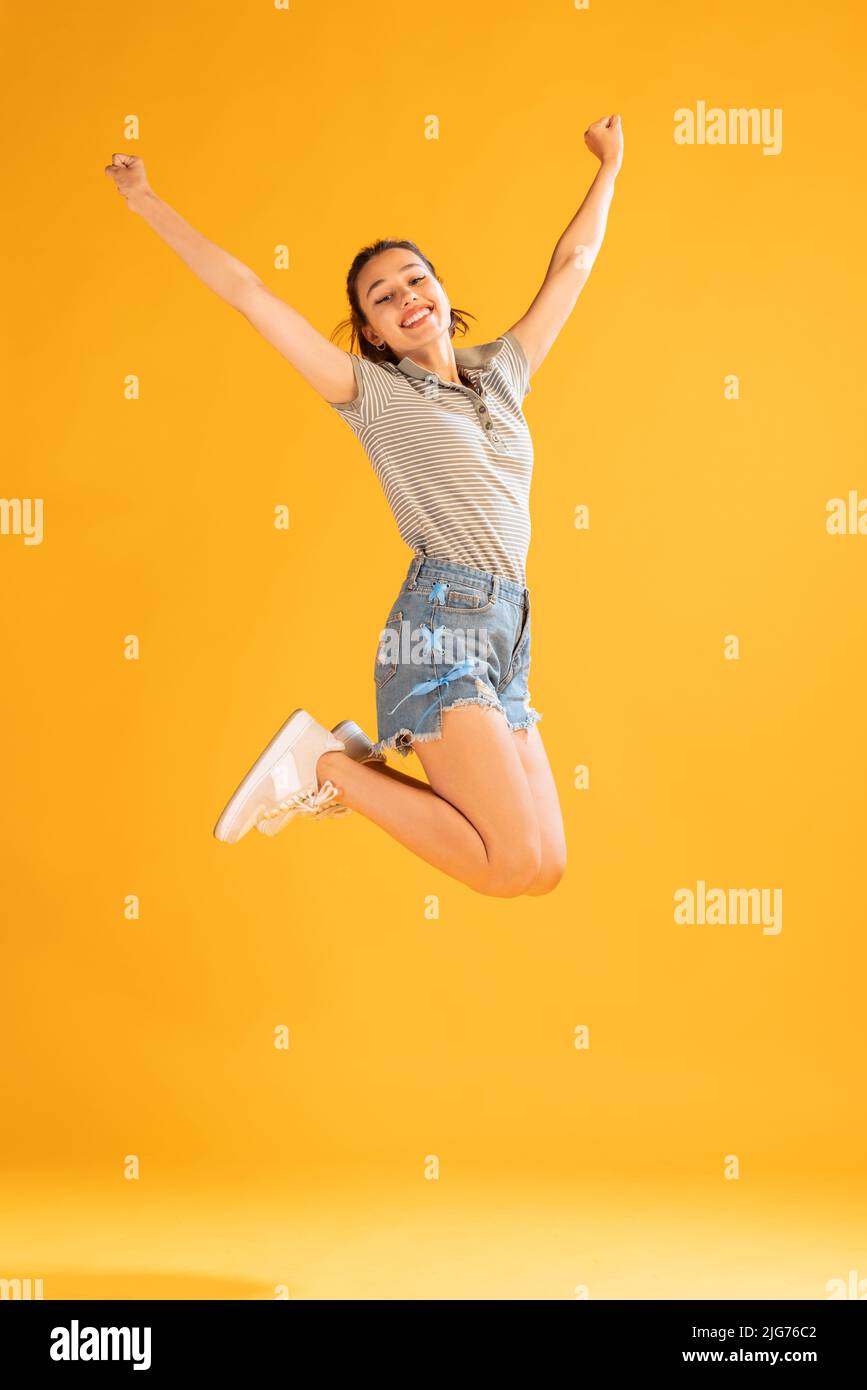 Full-length portrait of beautiful young girl in casual outfit jumping ...