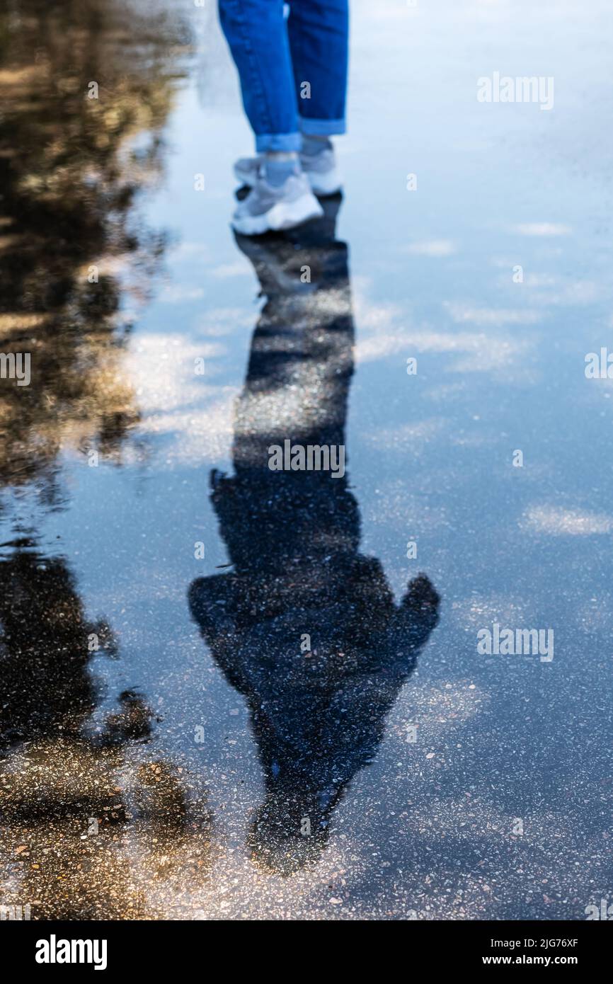 The silhouette of walking woman is reflected in a puddle on wet ...