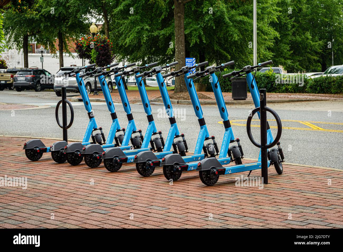 Eight blue scooters are lined up on a red brick sidewalk in an urban ...