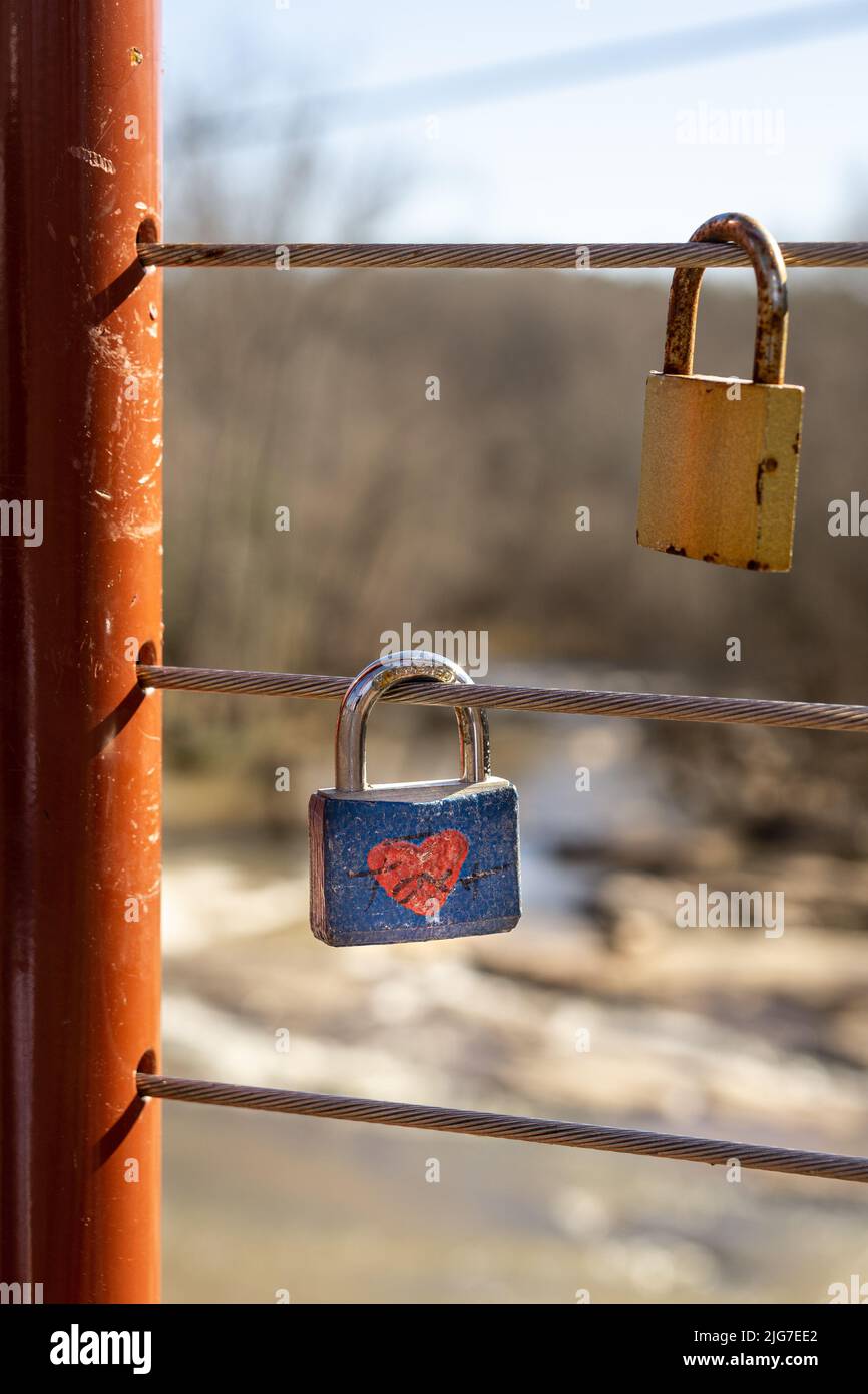 Two padlocks are hooked to the wire cables of a bridge above a river ...