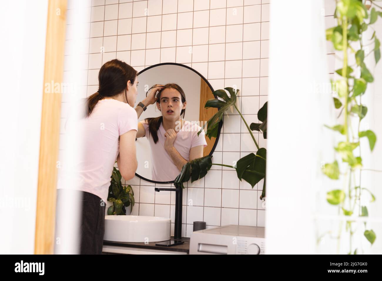 Image of caucasian non-binary trans woman looking at mirror in bathroom ...