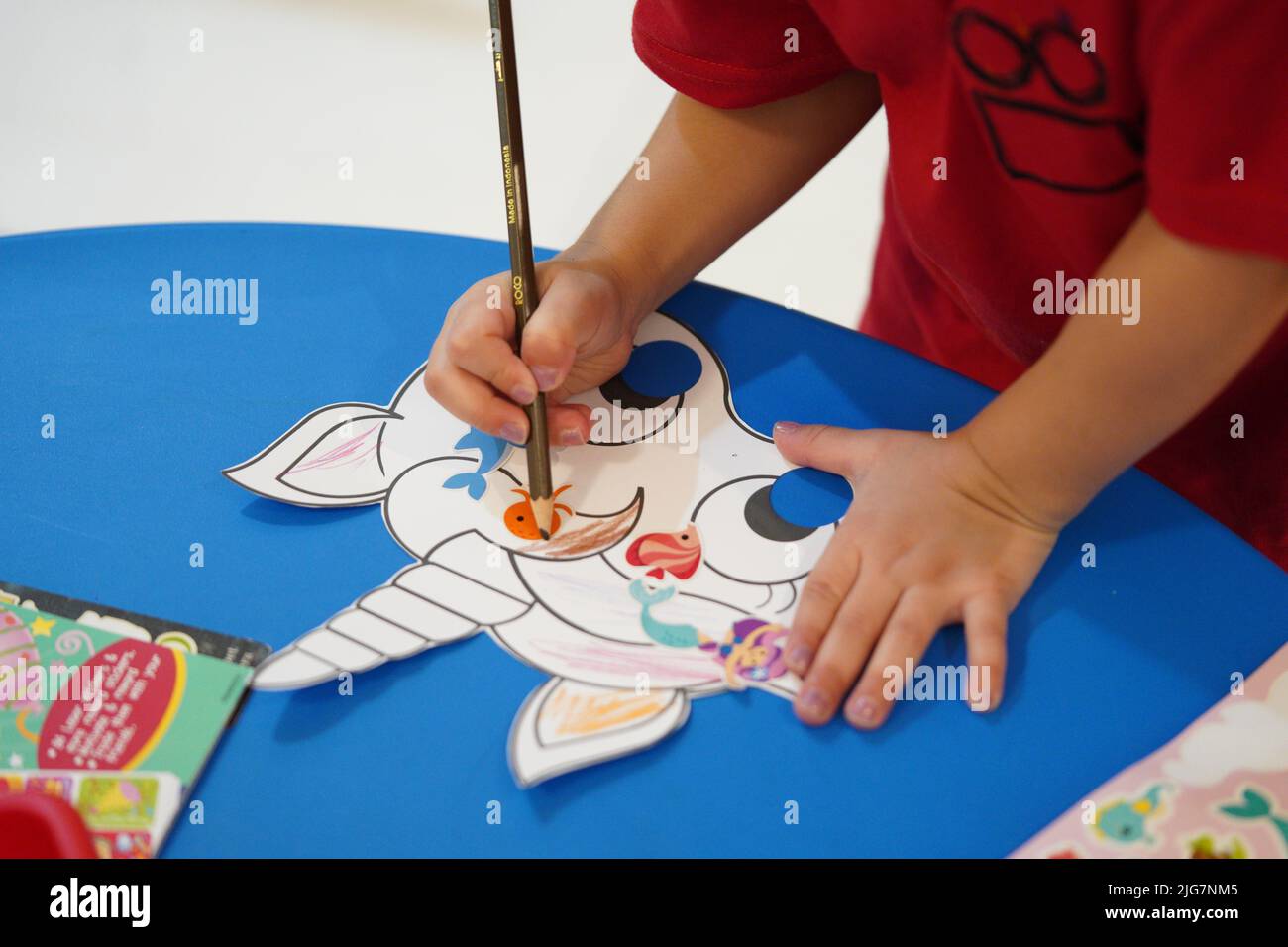 A little child coloring an animal paper mask in the classroom. Unicorn ...